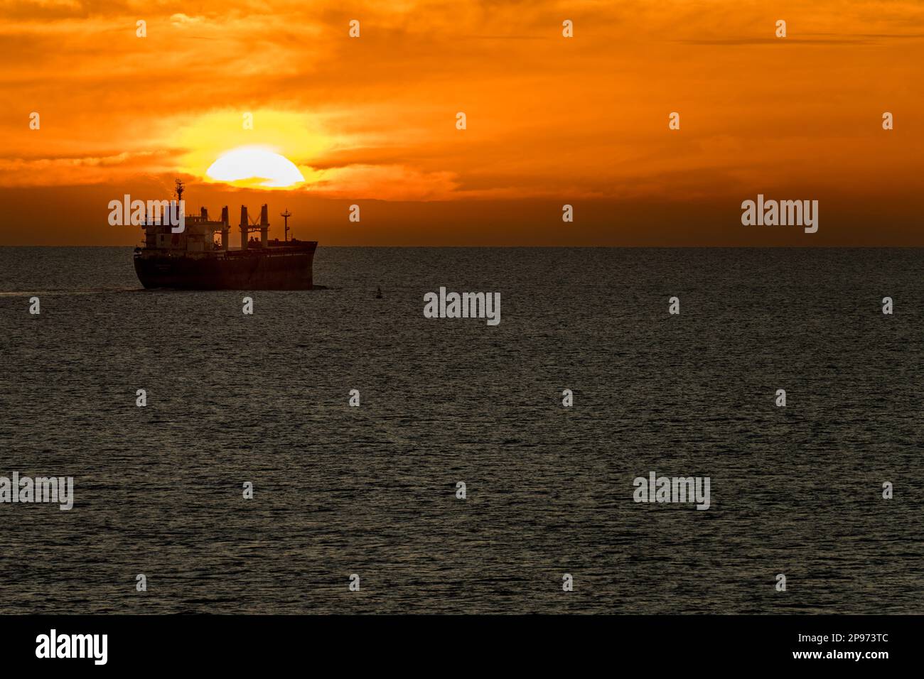 Sun setting over the water horizon with a bulk carrier cargo ship sailing away Stock Photo - Alamy