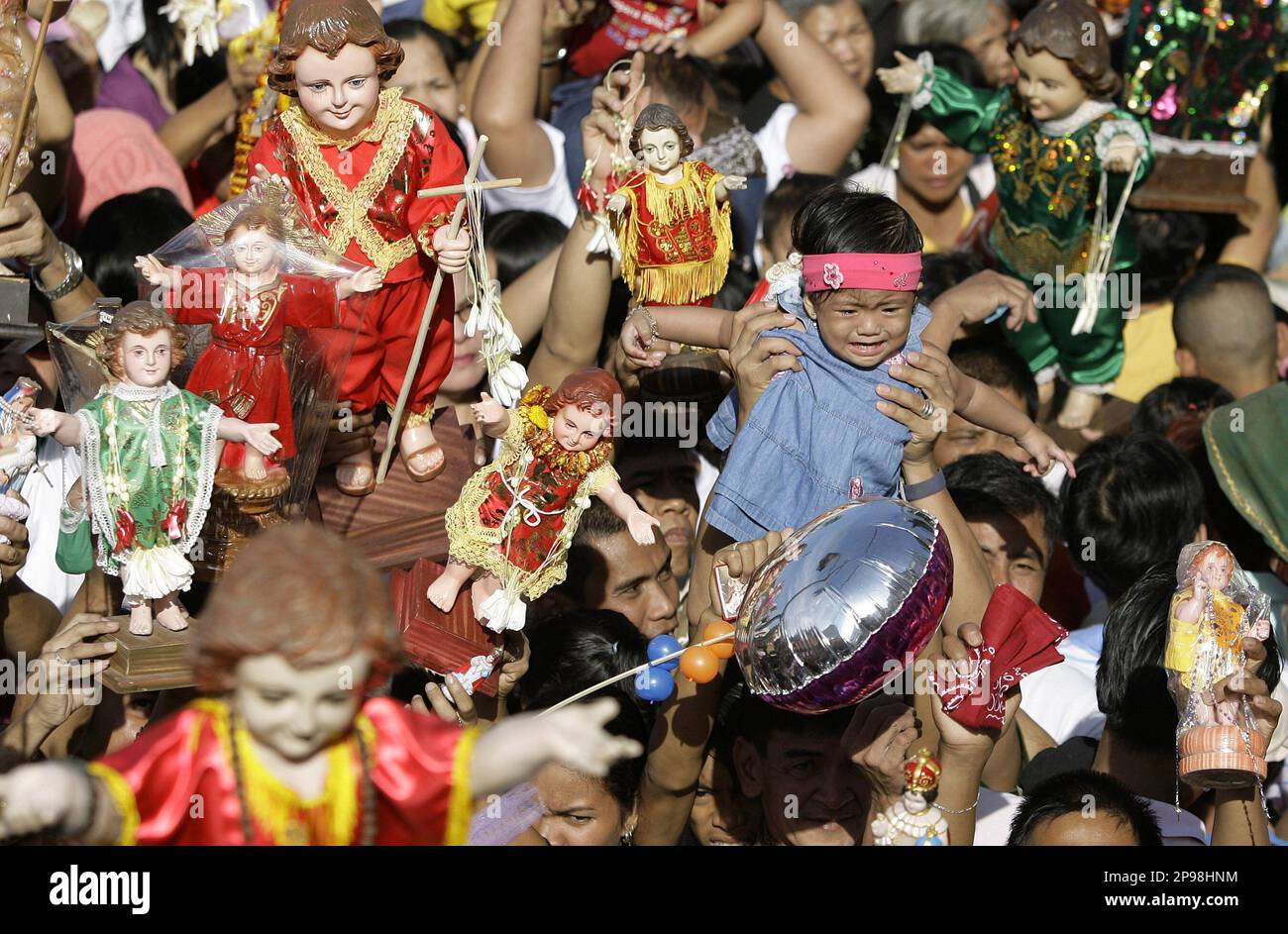A Filipino devotee carries a baby girl as others raise their statues of ...