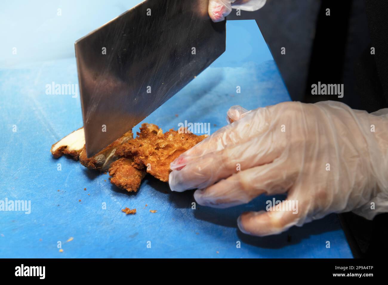 Chopping chicken in batter on a blue board with a kitchen machete in ...