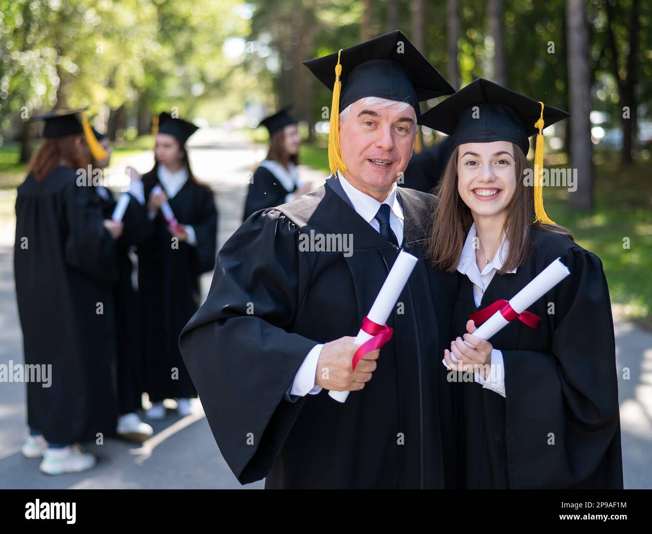 A group of graduates in robes outdoors. An elderly man and a young ...