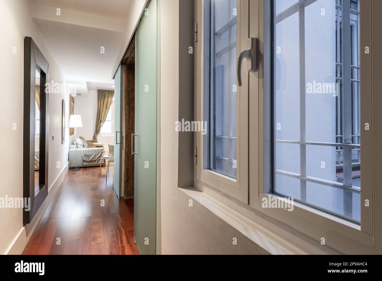 Corridor of a house with reddish wooden floors, aluminum windows with ...
