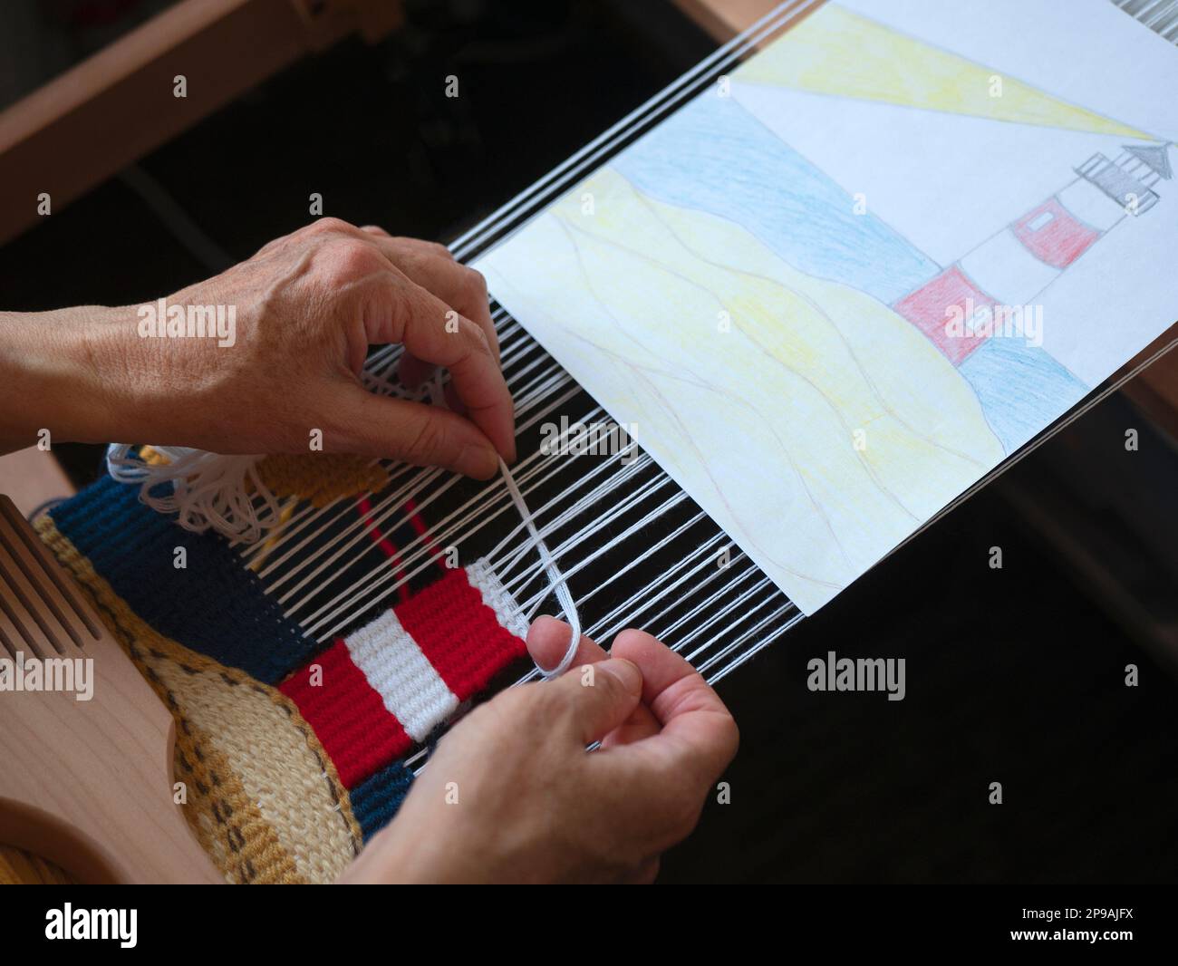 Weaver is making tapestry with lighthouse according to scheme. Hands in ...