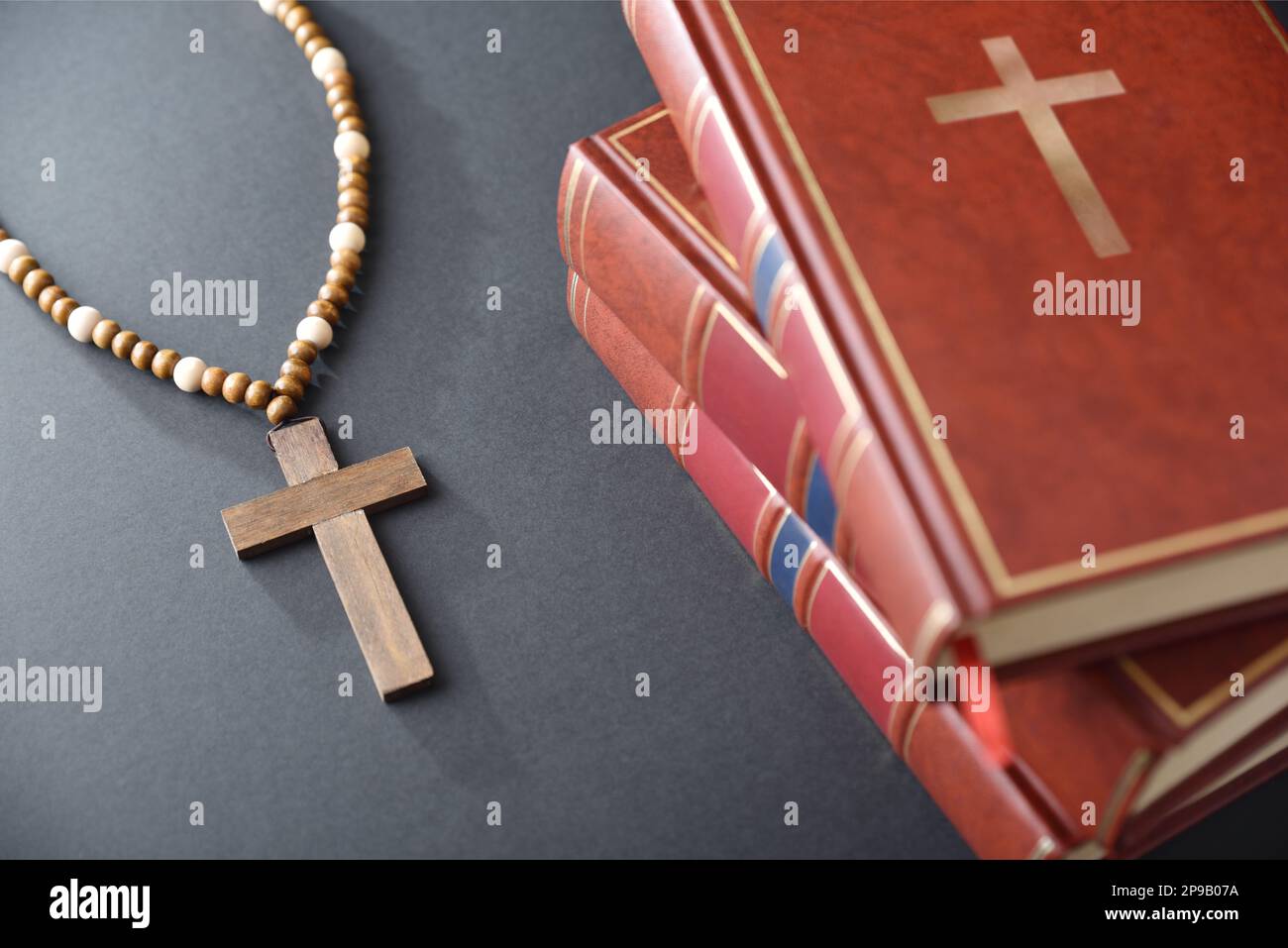Pile of religious books and cross with chain of wooden beads on black ...