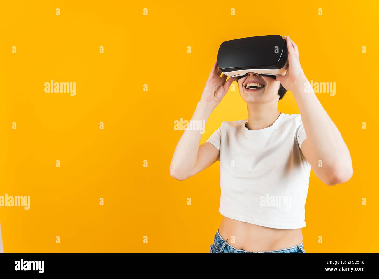 Woman smiling while using a virtual reality set. Orange background ...