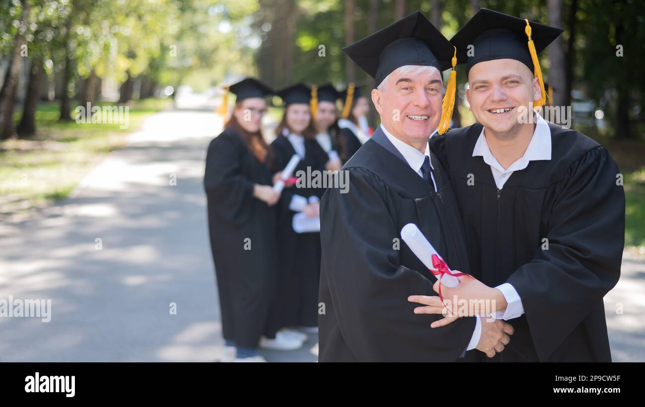 A group of graduates in robes outdoors. An elderly man and a young guy ...