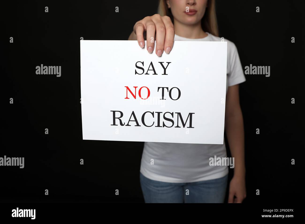 Young woman holding sign with phrase Say No To Racism on black ...
