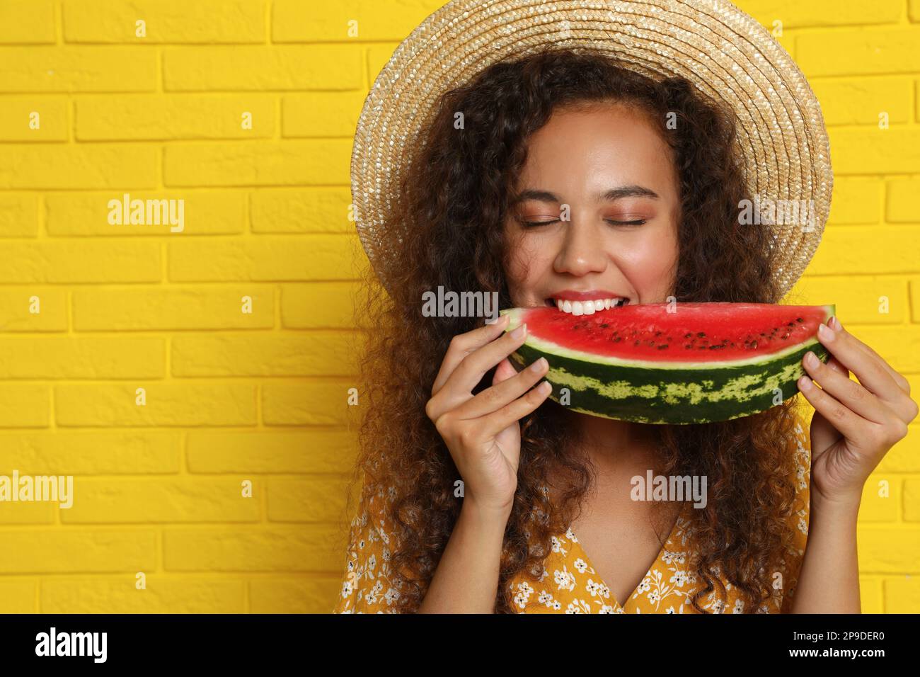 Beautiful young African American woman eating watermelon near yellow ...