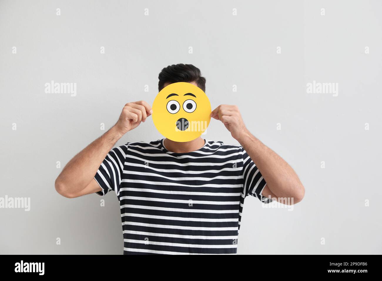 Man hiding emotions using card with drawn surprised face on white ...