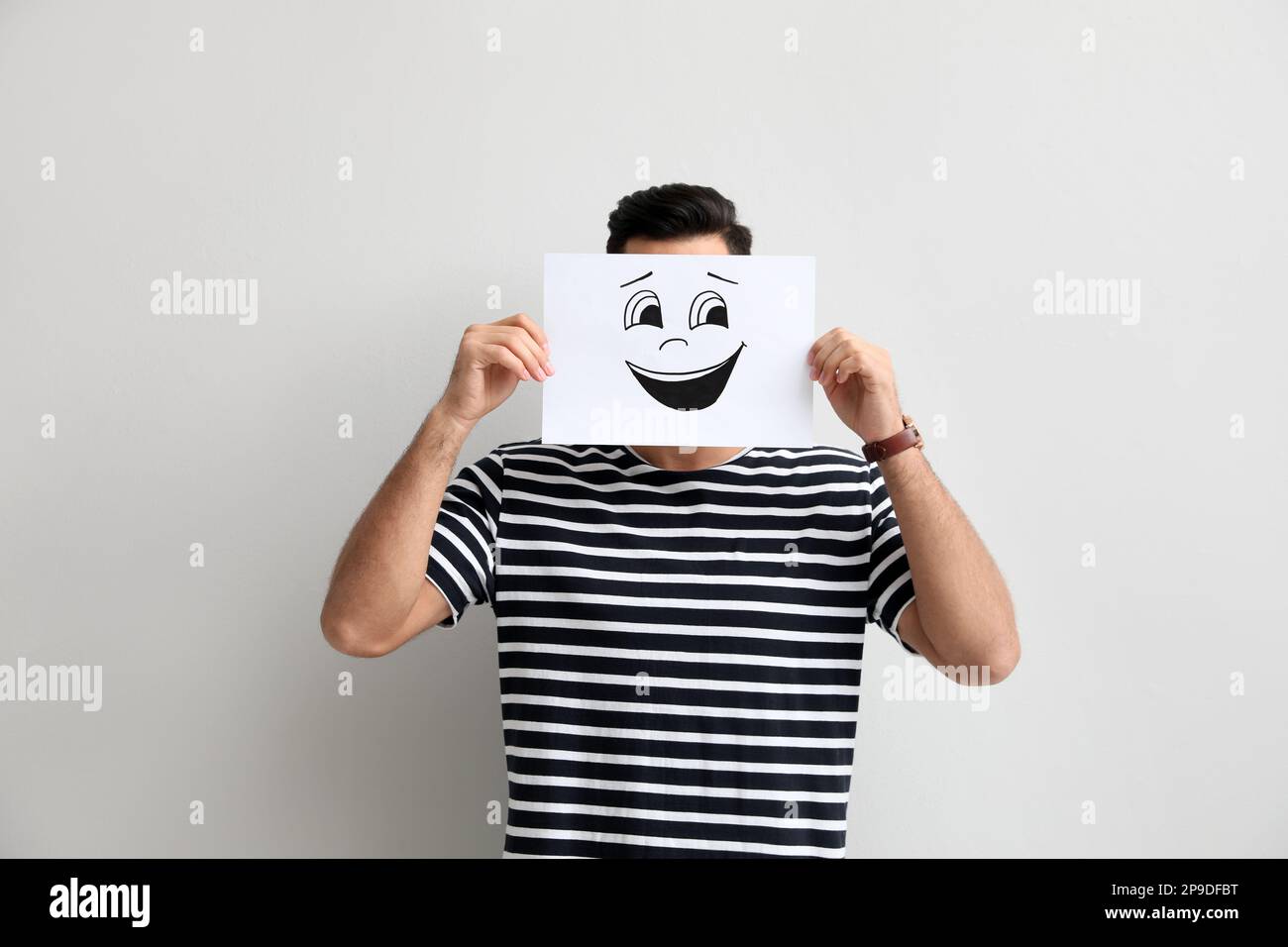 Man hiding emotions using card with drawn smiling face on white ...