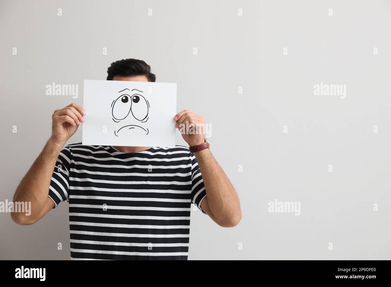 Man hiding emotions using card with drawn frowning face on white ...