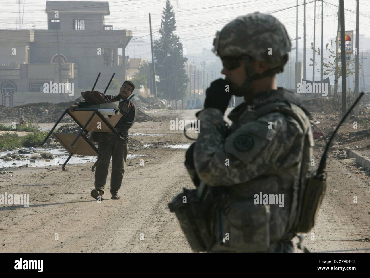 An Iraqi man carries office furniture as a U.S. Army soldier, of Iron ...