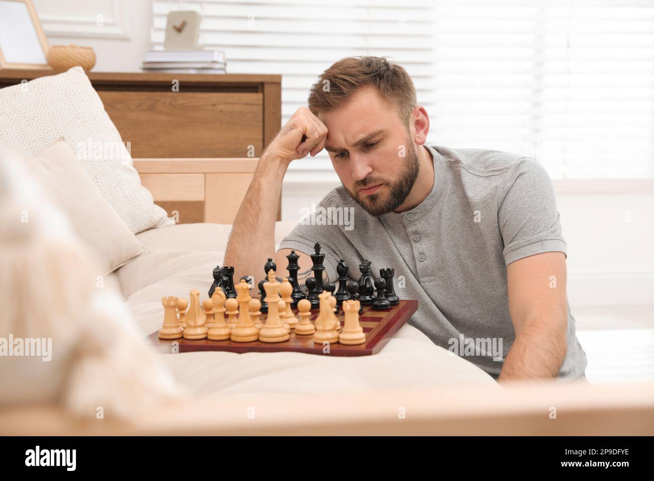 Thoughtful young man playing chess alone on sofa at home Stock Photo ...