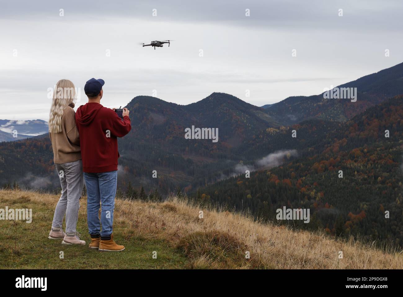 Young couple operating modern drone with remote control in mountains ...
