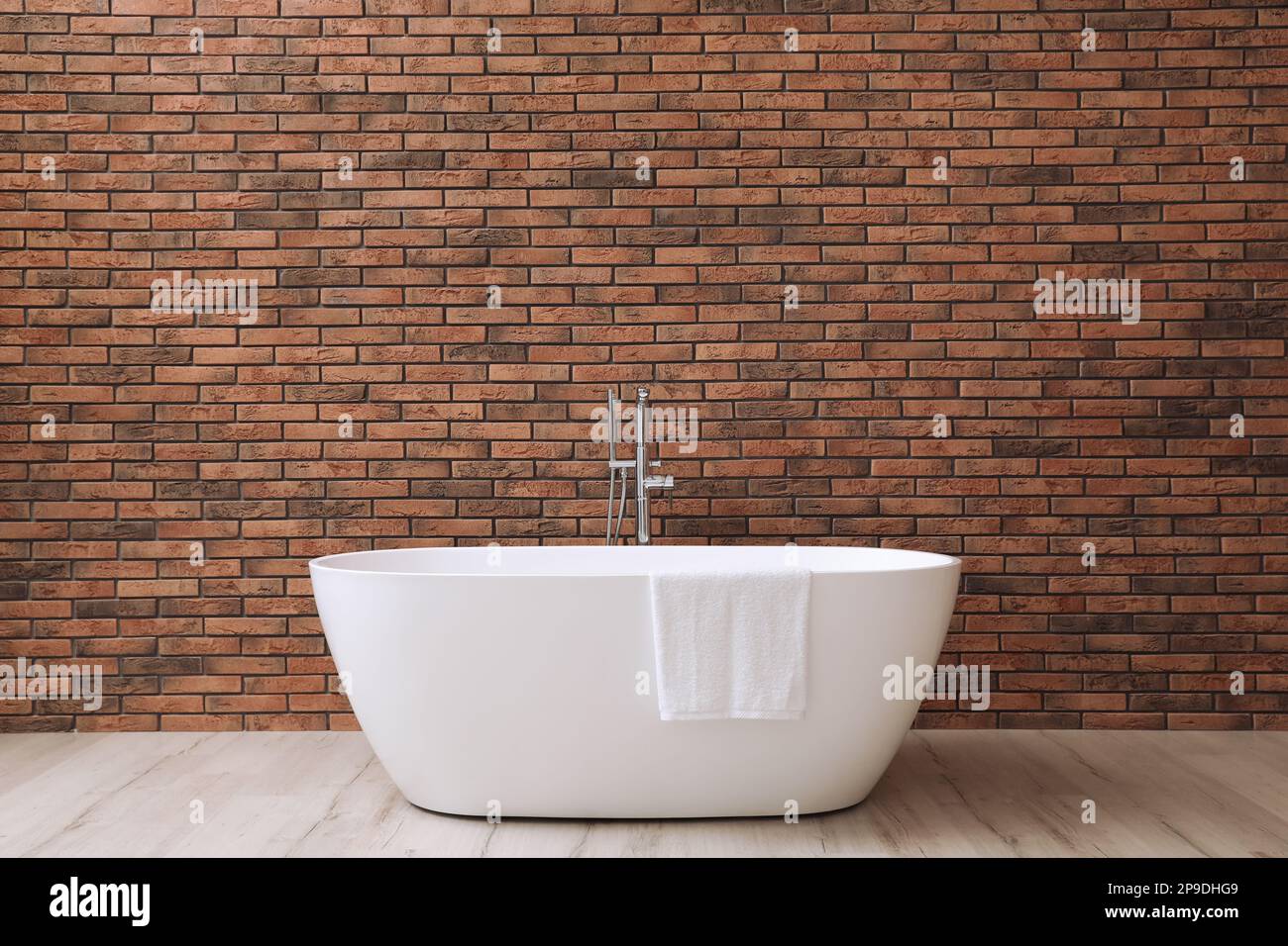 Modern ceramic bathtub with towel near brick wall Stock Photo - Alamy