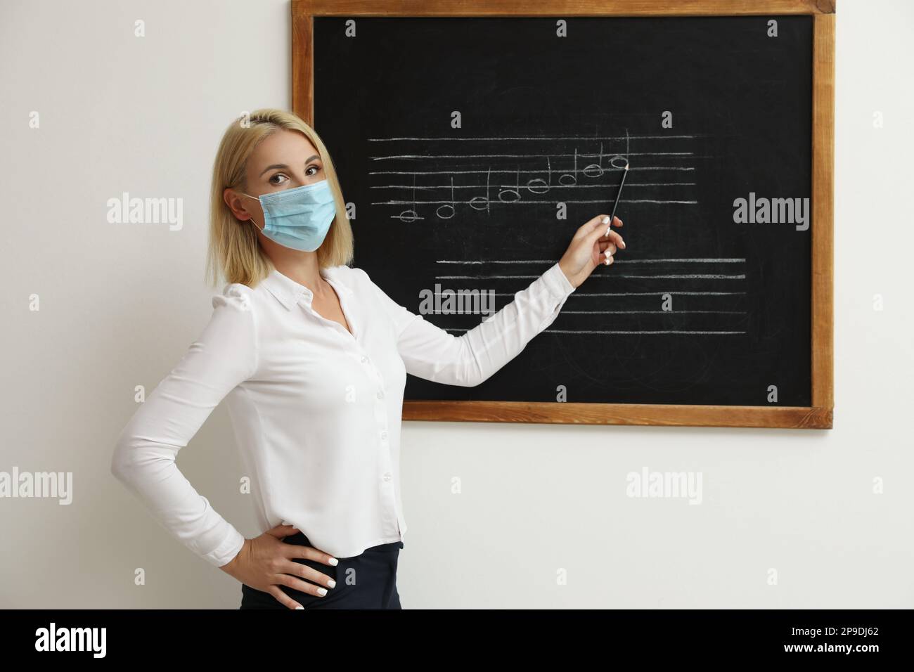 Teacher wearing protective mask near black chalkboard with music notes ...