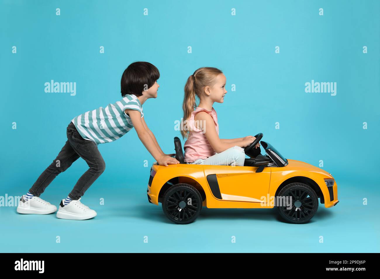 Cute boy pushing children's electric toy car with little girl on light ...