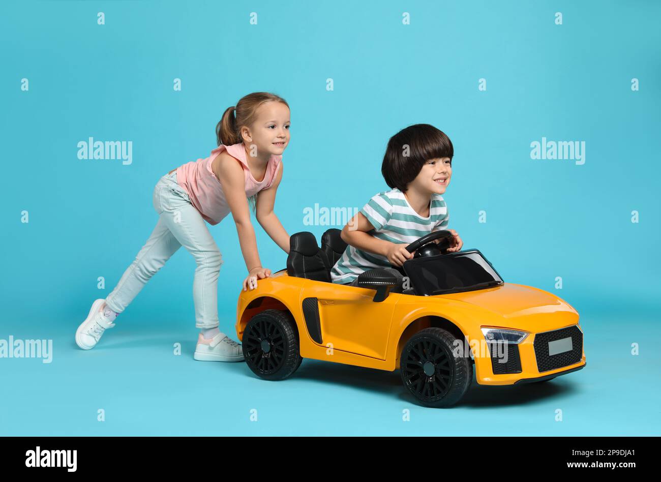 Cute girl pushing children's electric toy car with little boy on light ...