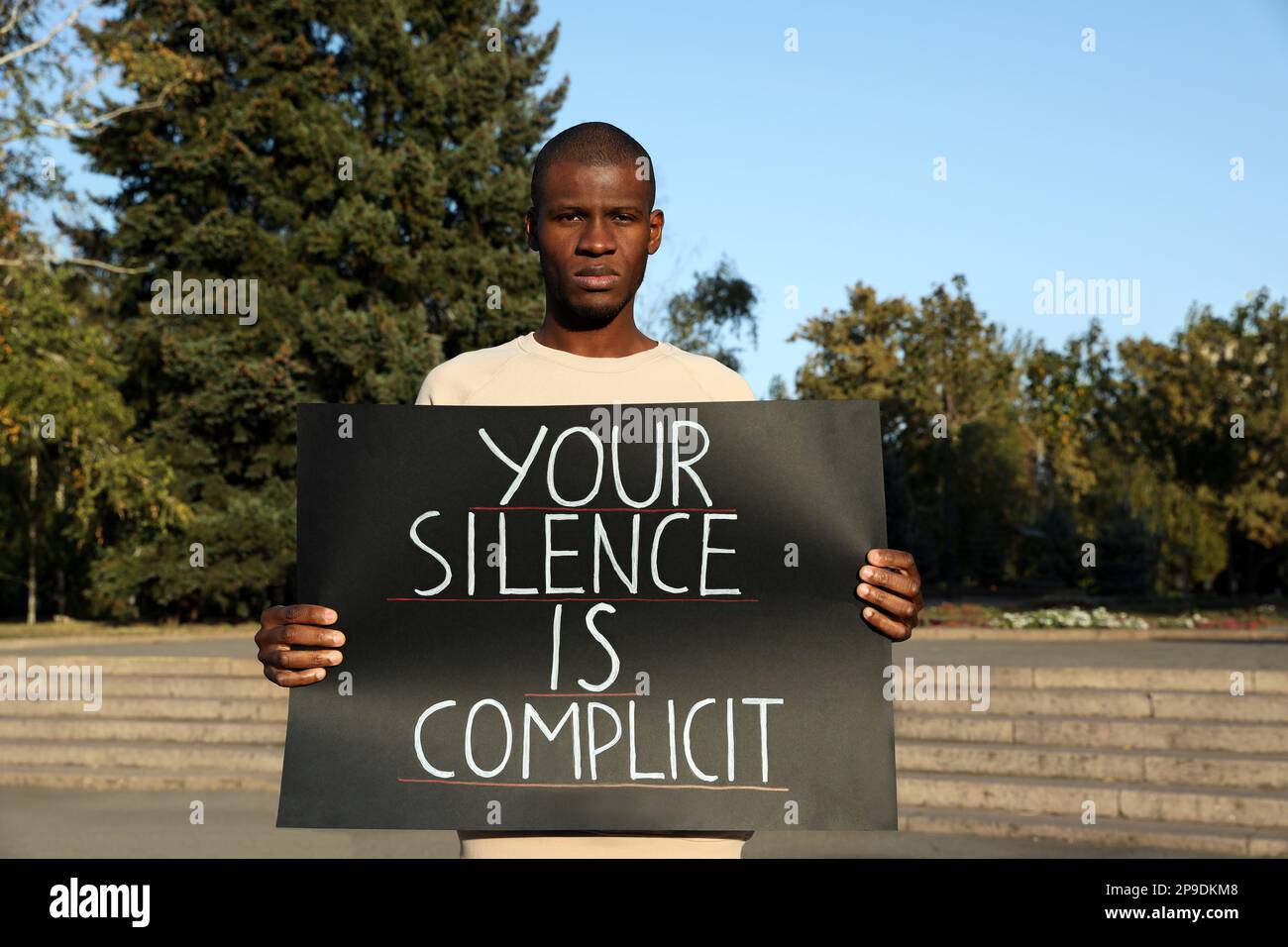 African American man holding sign with phrase Your Silence Is Complicit ...