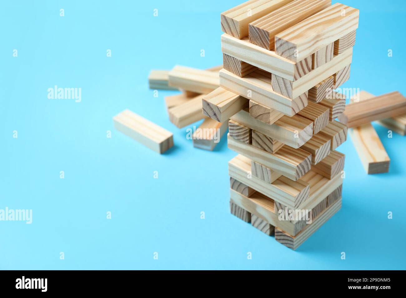 Jenga tower and wooden blocks on light blue background, space for text ...