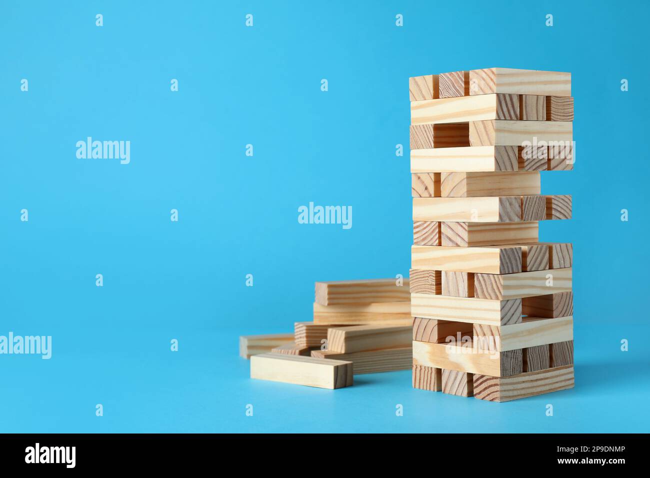 Jenga tower and wooden blocks on light blue background, space for text ...