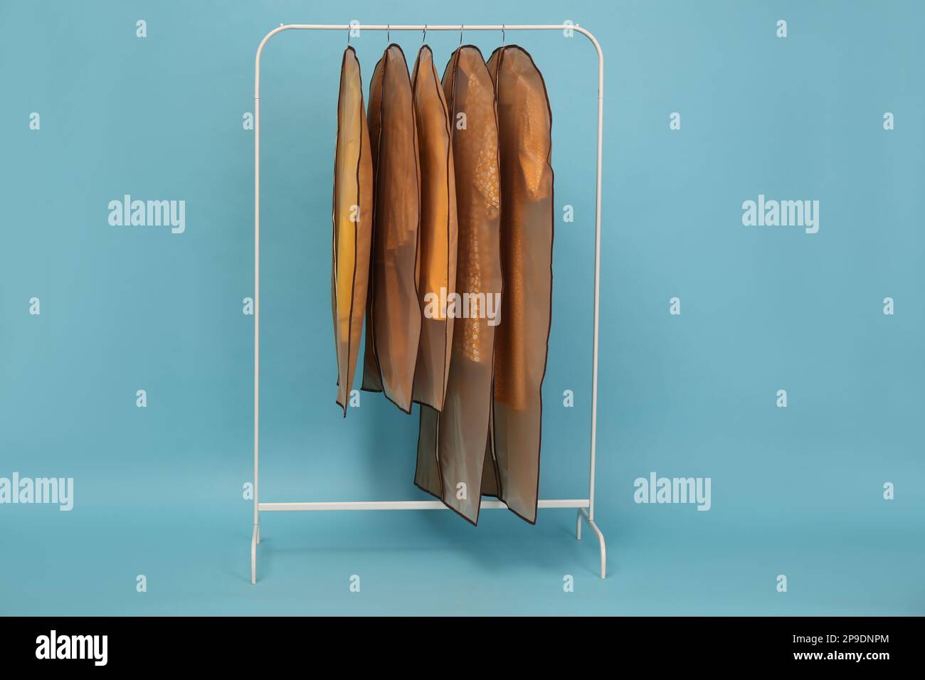 Garment bags with clothes on rack against light blue background Stock ...