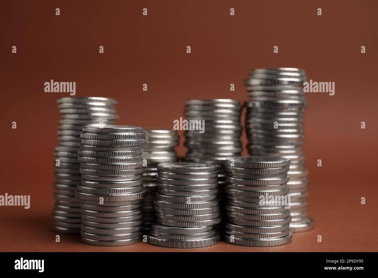 Many silver coins stacked on brown background Stock Photo - Alamy