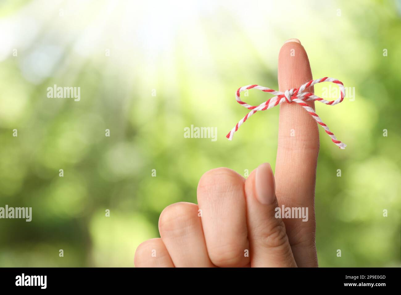 Woman showing index finger with tied bow as reminder on blurred green ...