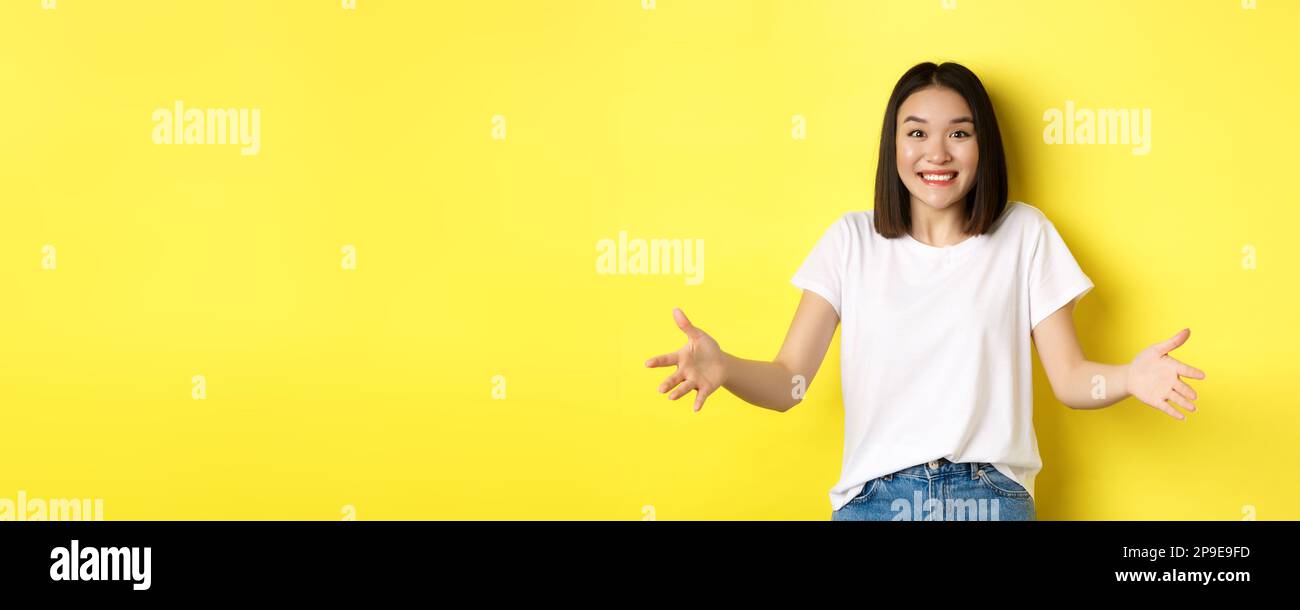 Cheerful asian girl holding something large and long, smiling happy at ...