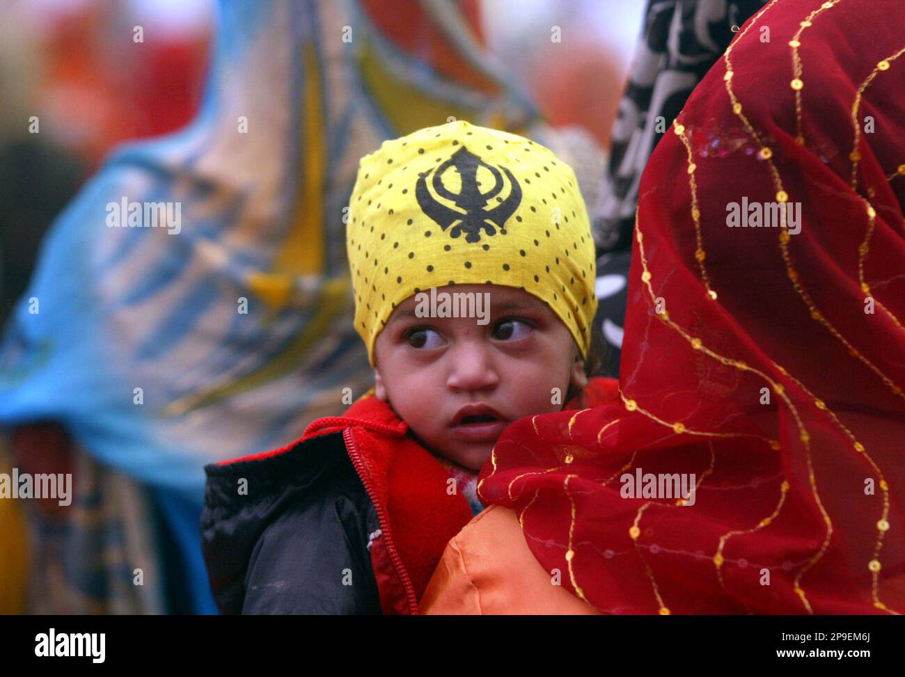 A child wears a scarf displaying the Sikh symbol, as elders look on ...