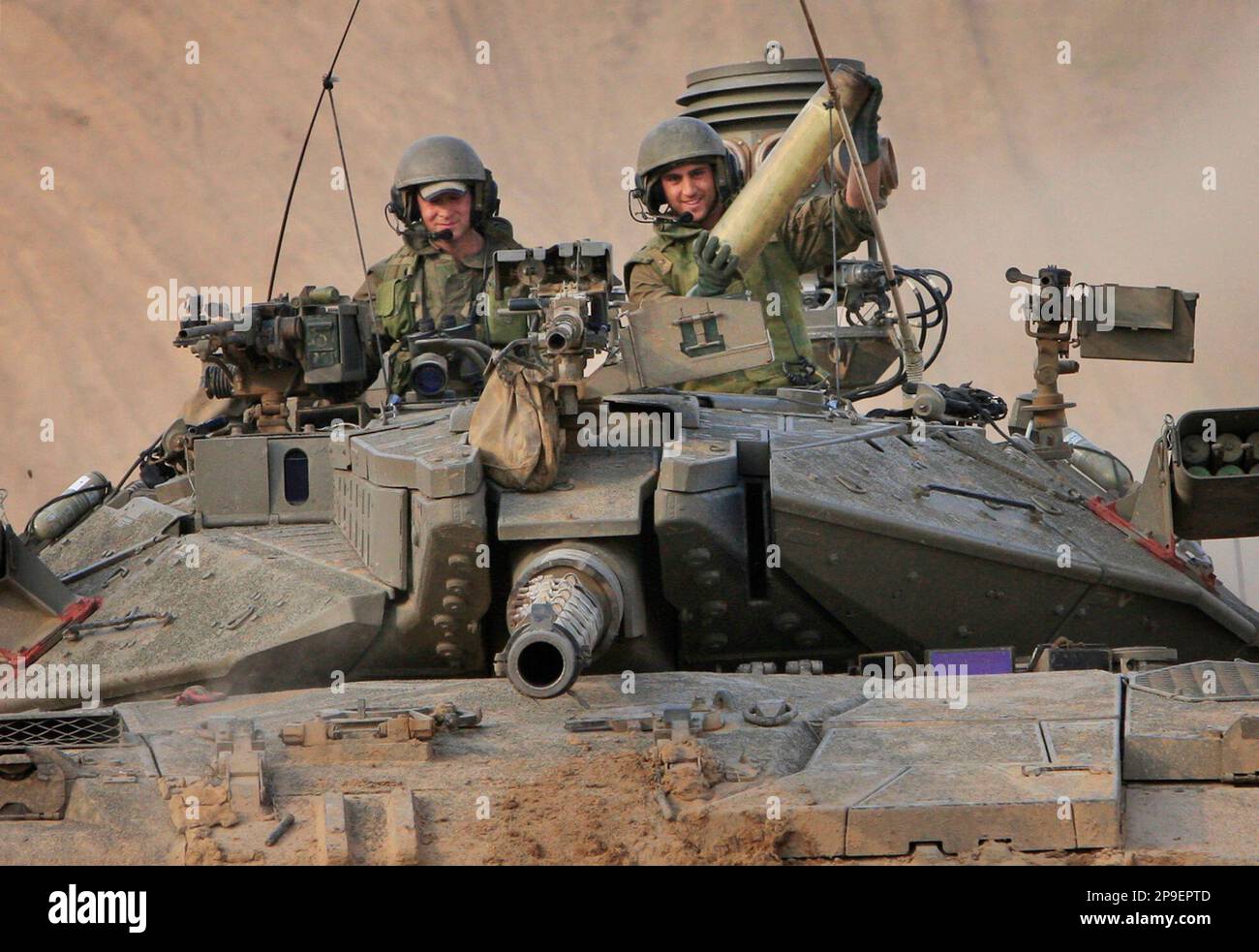 An Israeli tank crew member lifts up a spent shell as they drive along ...