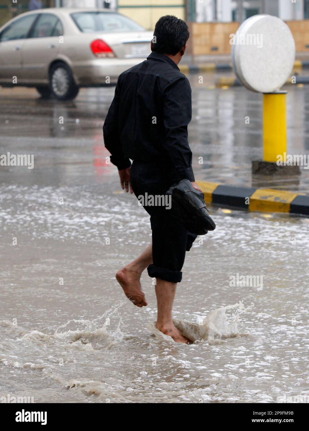 A barefoot man with rolled up trousers crosses a flooded street in ...