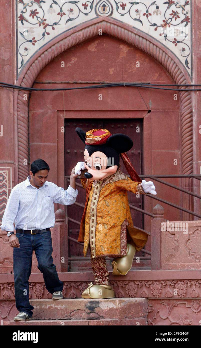 A man helps Walt Disney cartoon character Mickey Mouse walk down a set ...