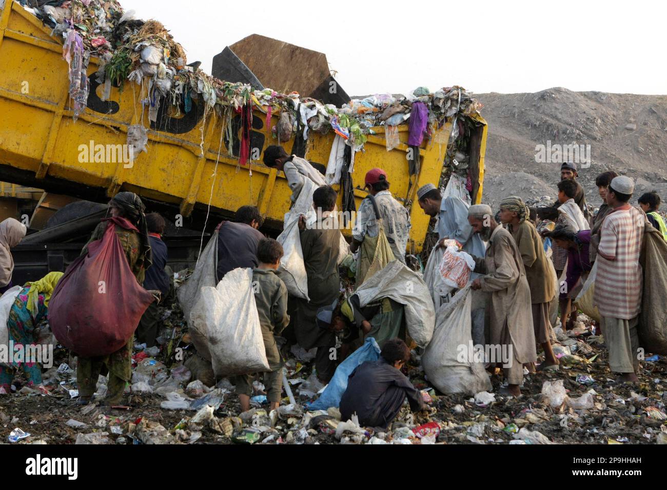 Pakistani scavengers surround a garbage truck to collect recyclable ...