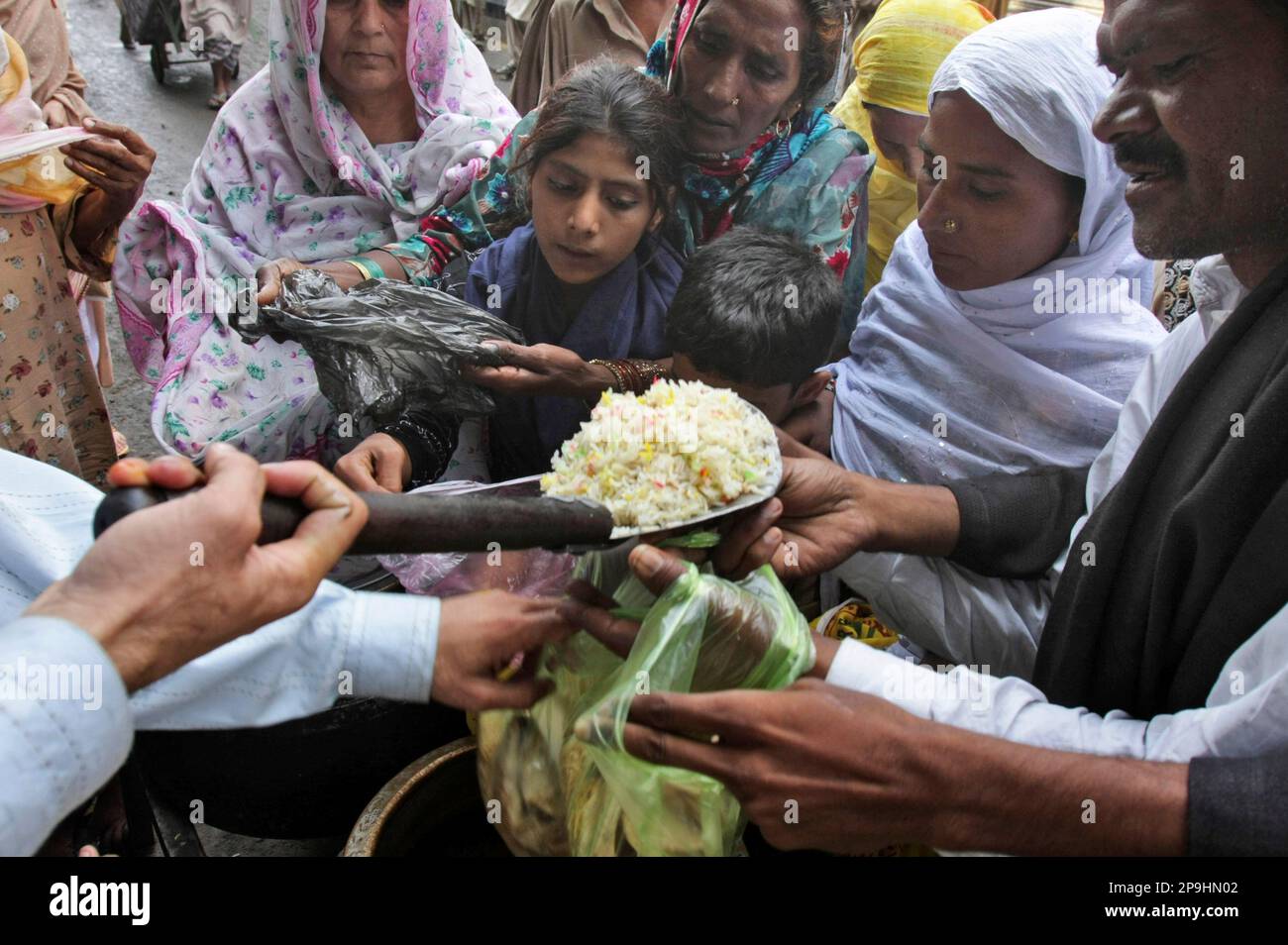 Pakistani people receive their donated food in a food distribution ...