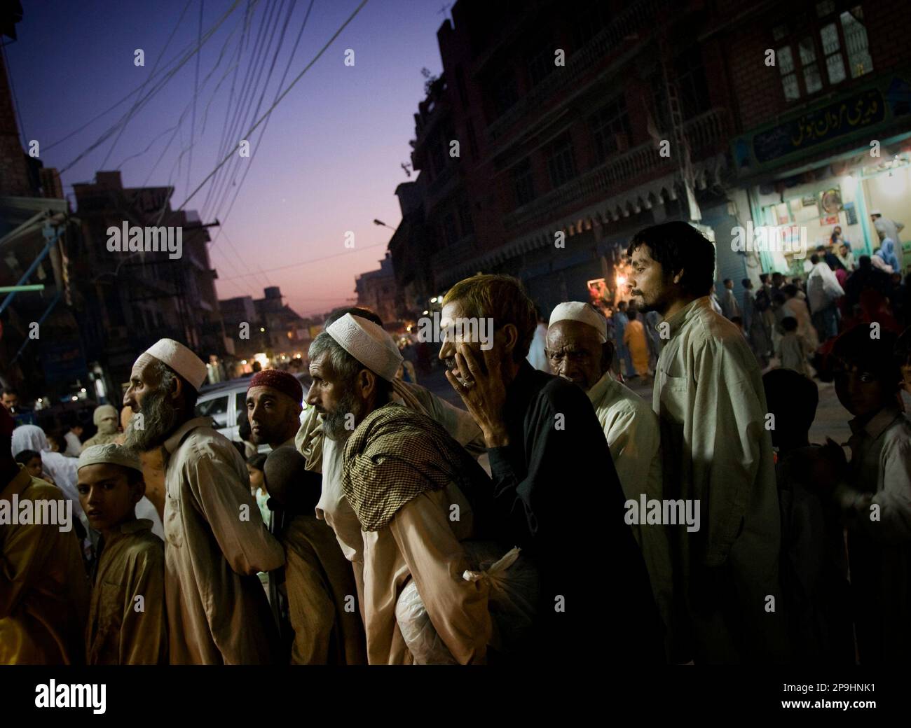 Pakistani men line up as they wait for their donated food in a food ...