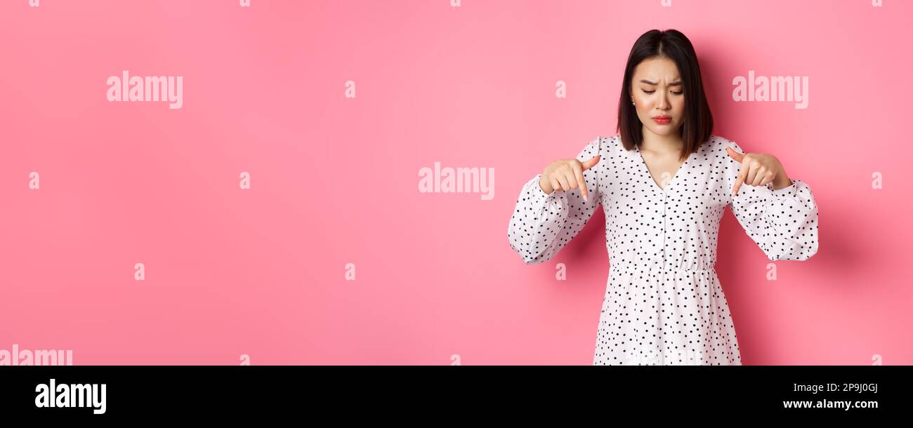 Concerned asian woman peeking down and pointing hand at disturbing ...