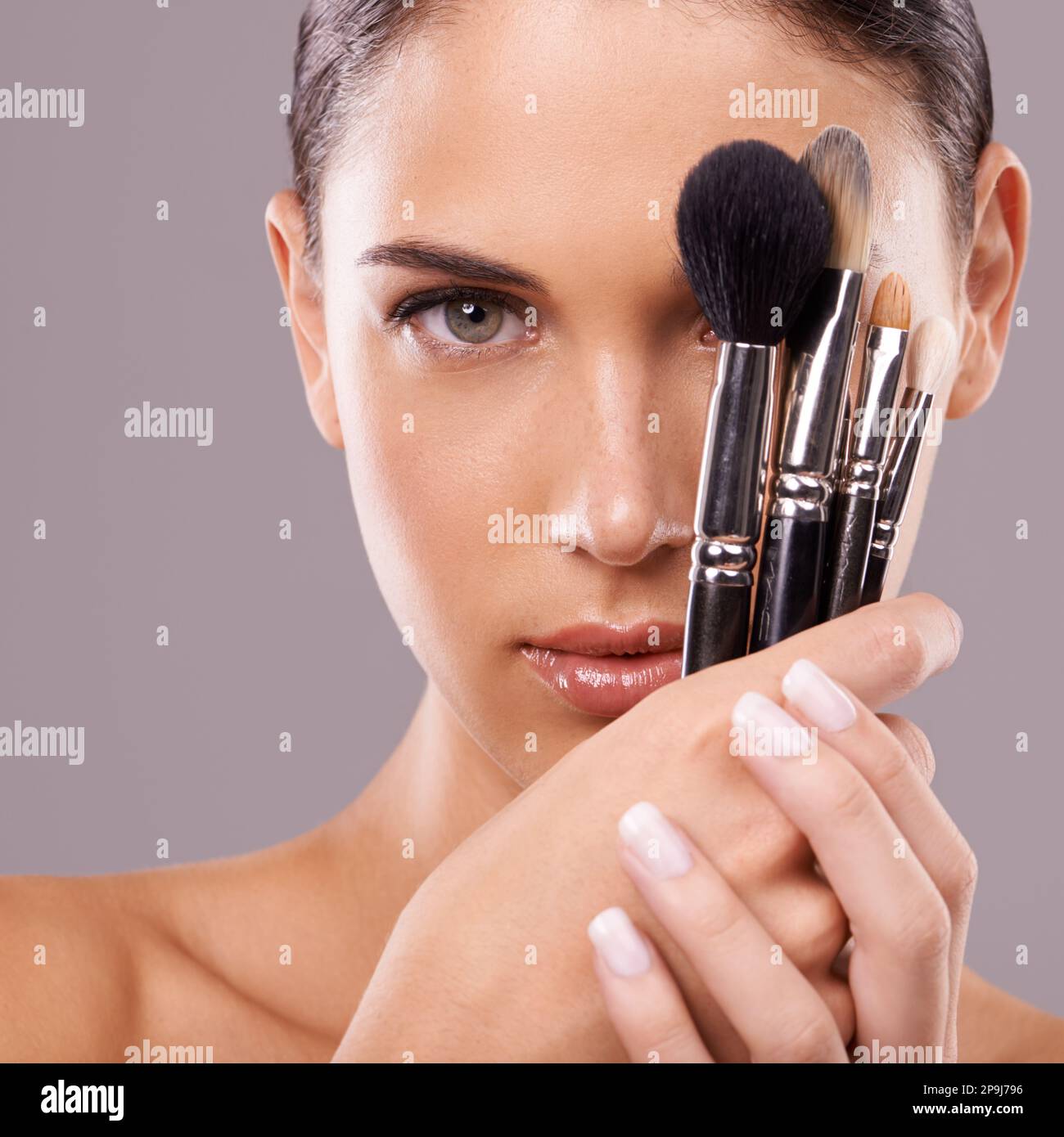 Tools of the trade. A young woman holding makeup brushes against her ...