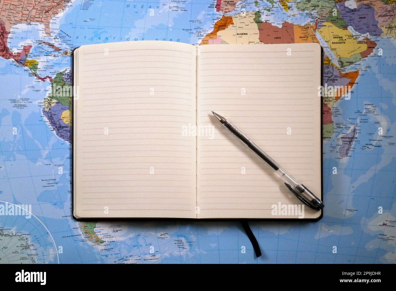 World map with on it an open note pad with a ballpoint pen on atop of ...