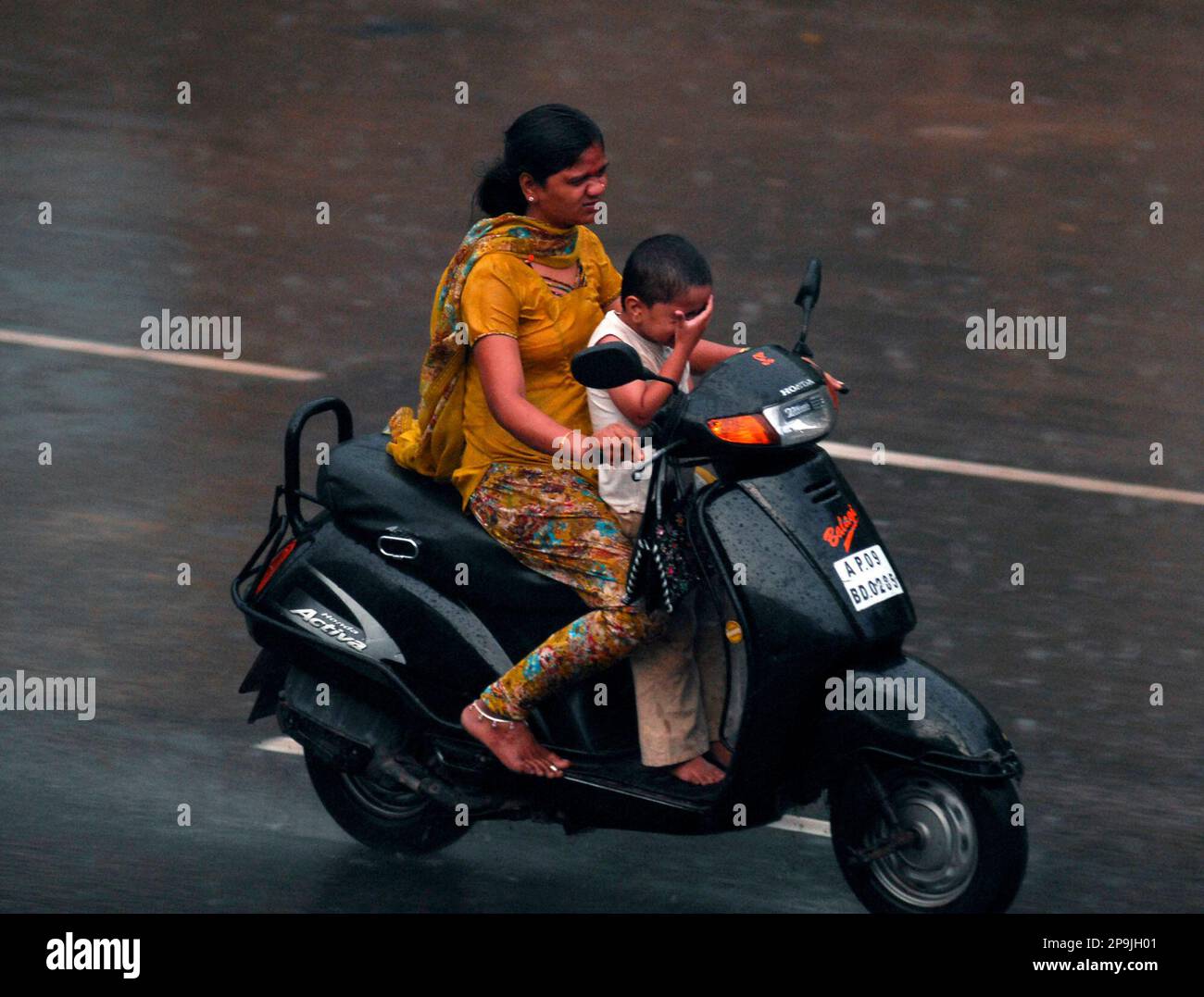 A woman and her son take a ride in a two-wheeler, as it rains in ...