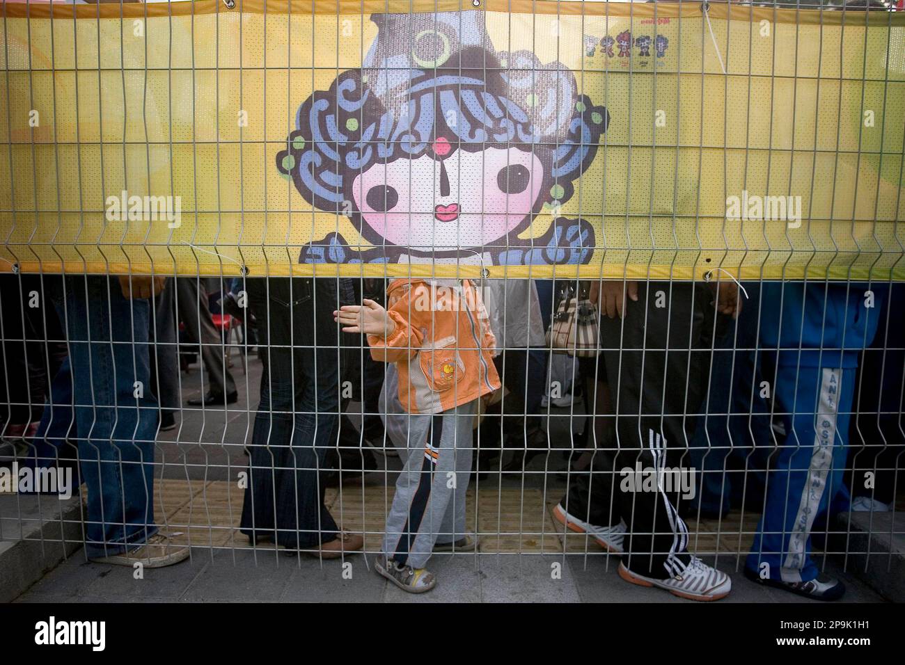 A Chinese child, center, passes by a poster that shows Fuwa Beibei, one ...