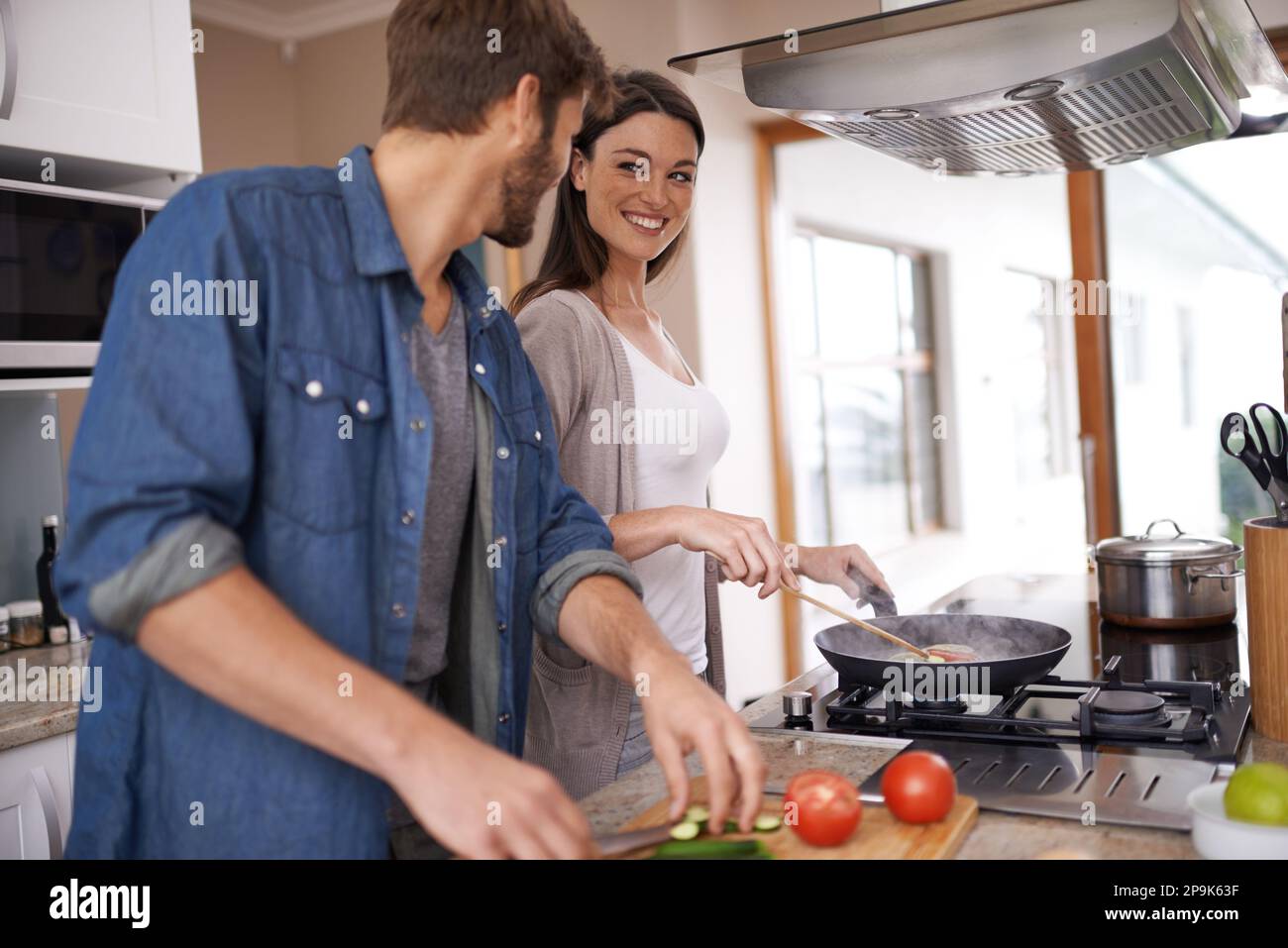 Lending a helping hand. A young couple making dinner together at home ...