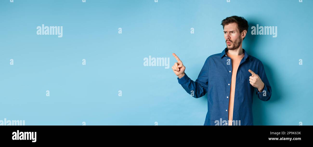 Confused and annoyed guy pointing and looking left at empty space with ...