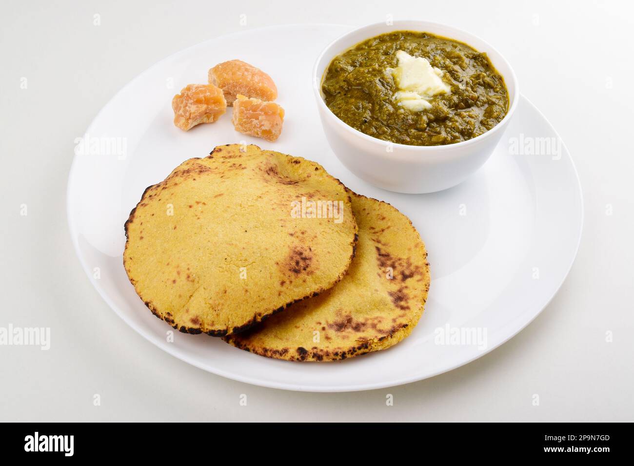 Sarso saag with makki roti served with jaggery in white plate isolated ...