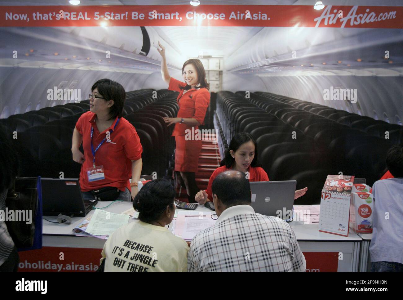 A staff attends to customers, foreground, at AirAsia's booth during the ...