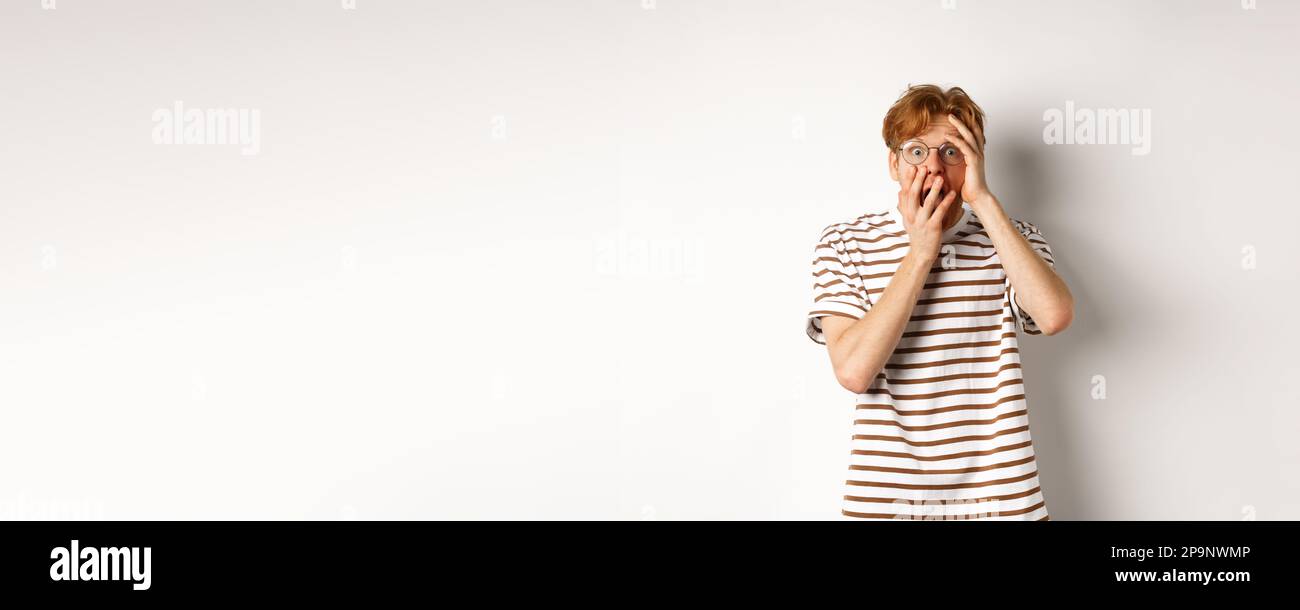 Scared redhead guy screaming terrified, holding hands on face from fear ...