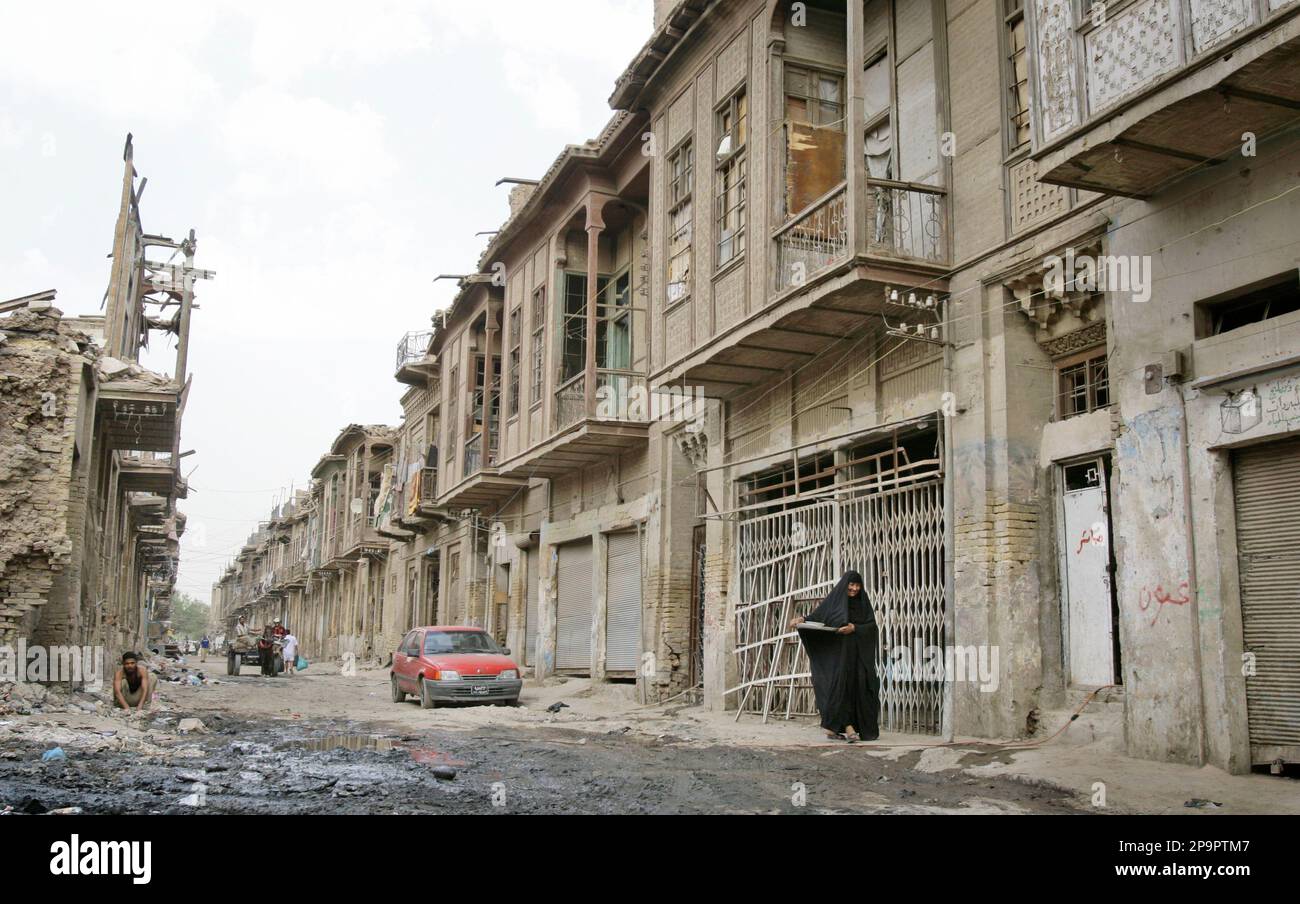 An elderly Iraqi woman carries dishes past old houses in a formerly ...