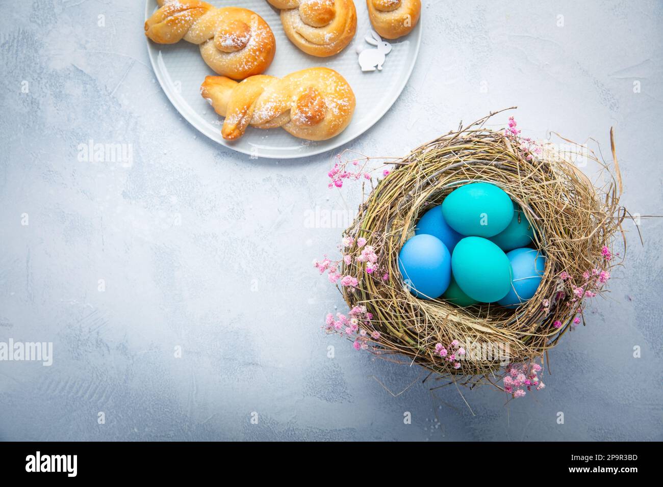 Easter eggs in nest with sweet buns made from yeast dough in a shape of ...