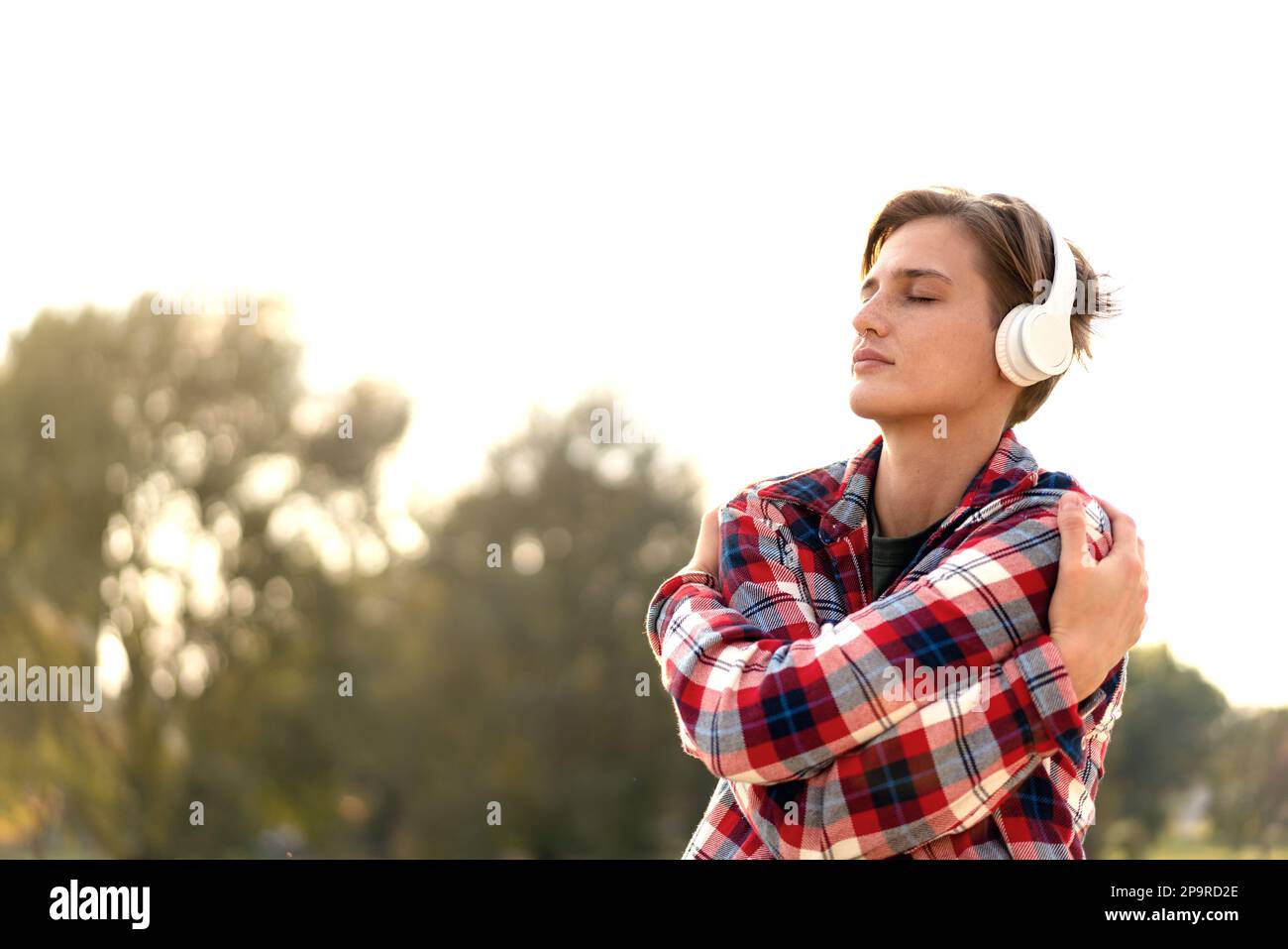 Young urban woman in headphones breathing fresh air and self hugging ...