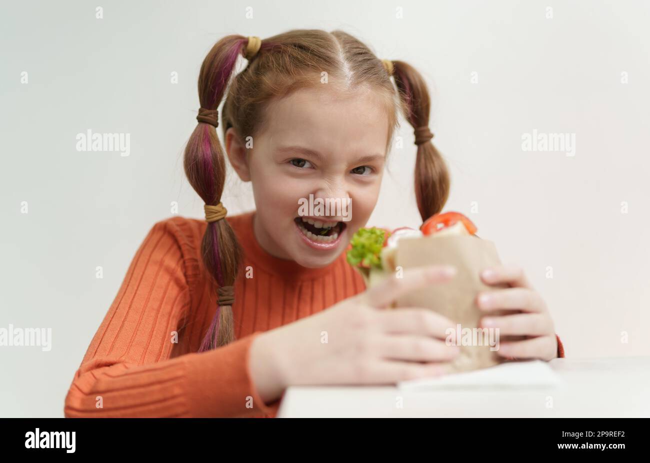 Portrait of funny little girl biting sandwich with a grin on her face ...
