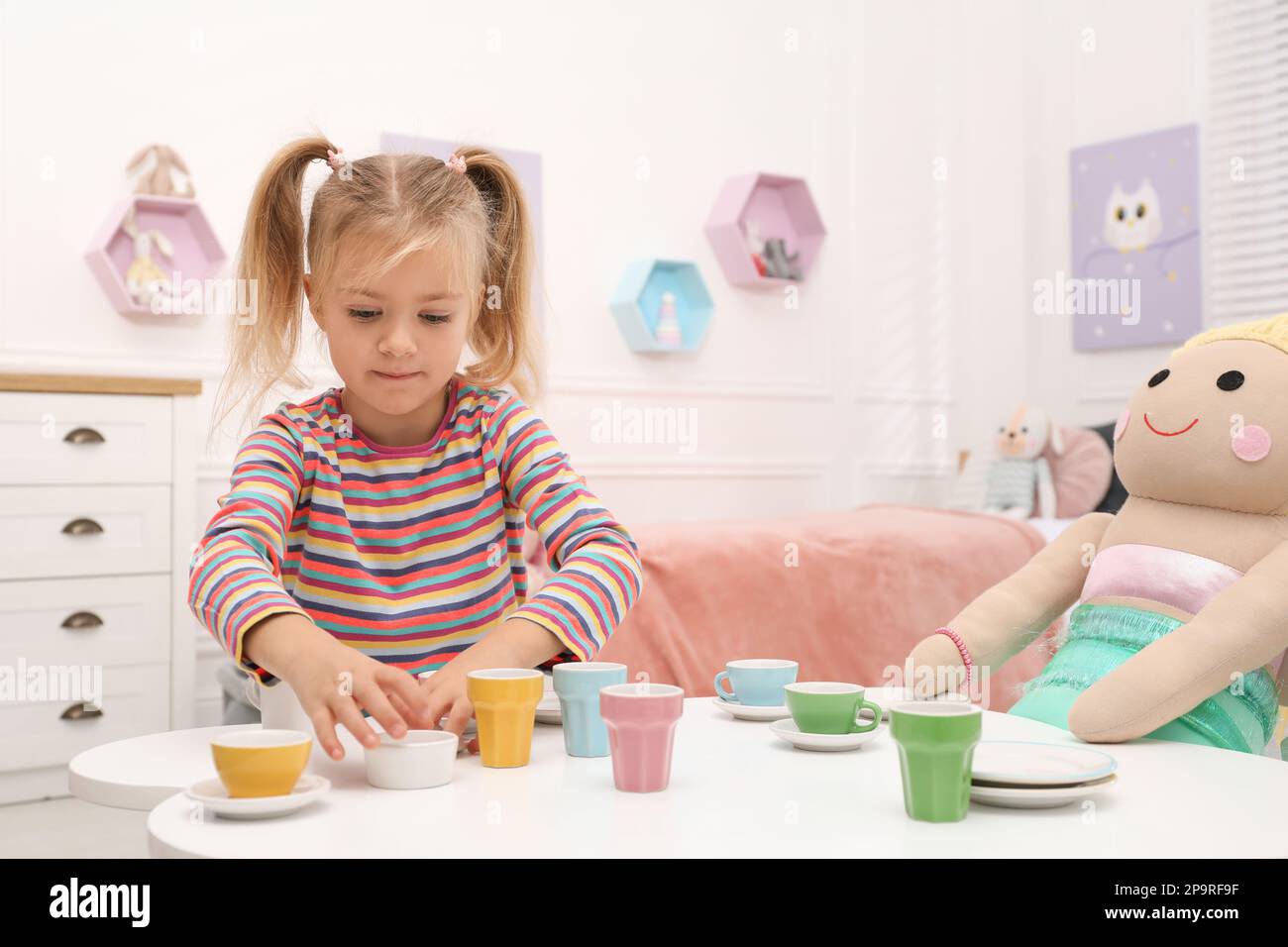Cute little girl playing tea party with doll at table in room Stock ...